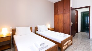 Quarto de hotel com duas camas de solteiro, armários de madeira, mesas de cabeceira com luminárias e uma porta que dá para outro quarto.
