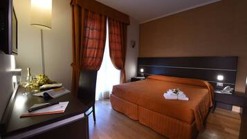 Quarto de hotel com cama, escrivaninha, luminária e telefone.