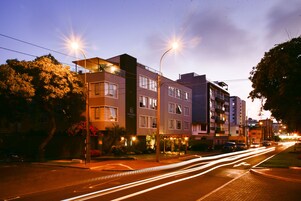 Um hotel com vários andares, entrada coberta e uma rua bem iluminada em primeiro plano.