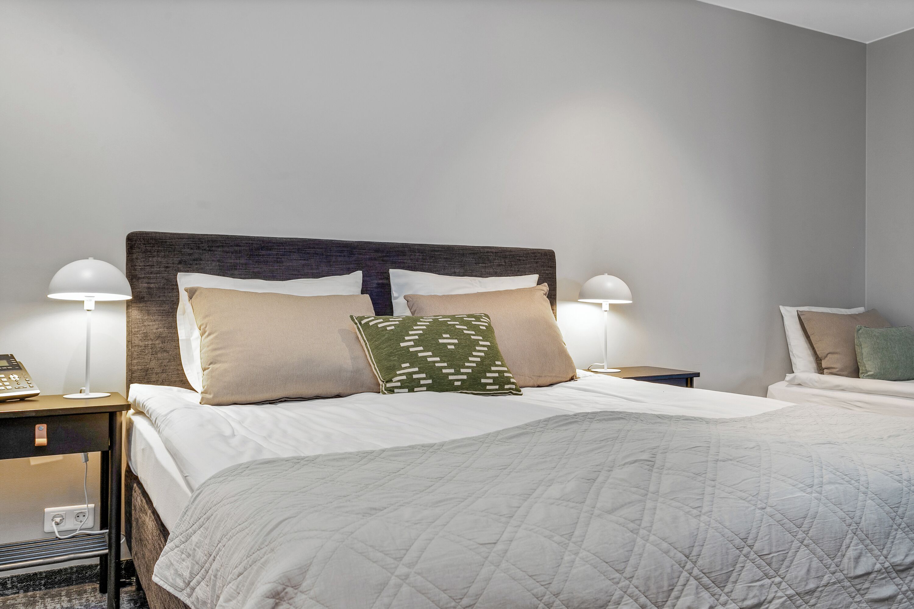 Uma cama bem arrumada com um edredom acolchoado, duas luminárias de cabeceira e uma mesa de cabeceira com abajur.