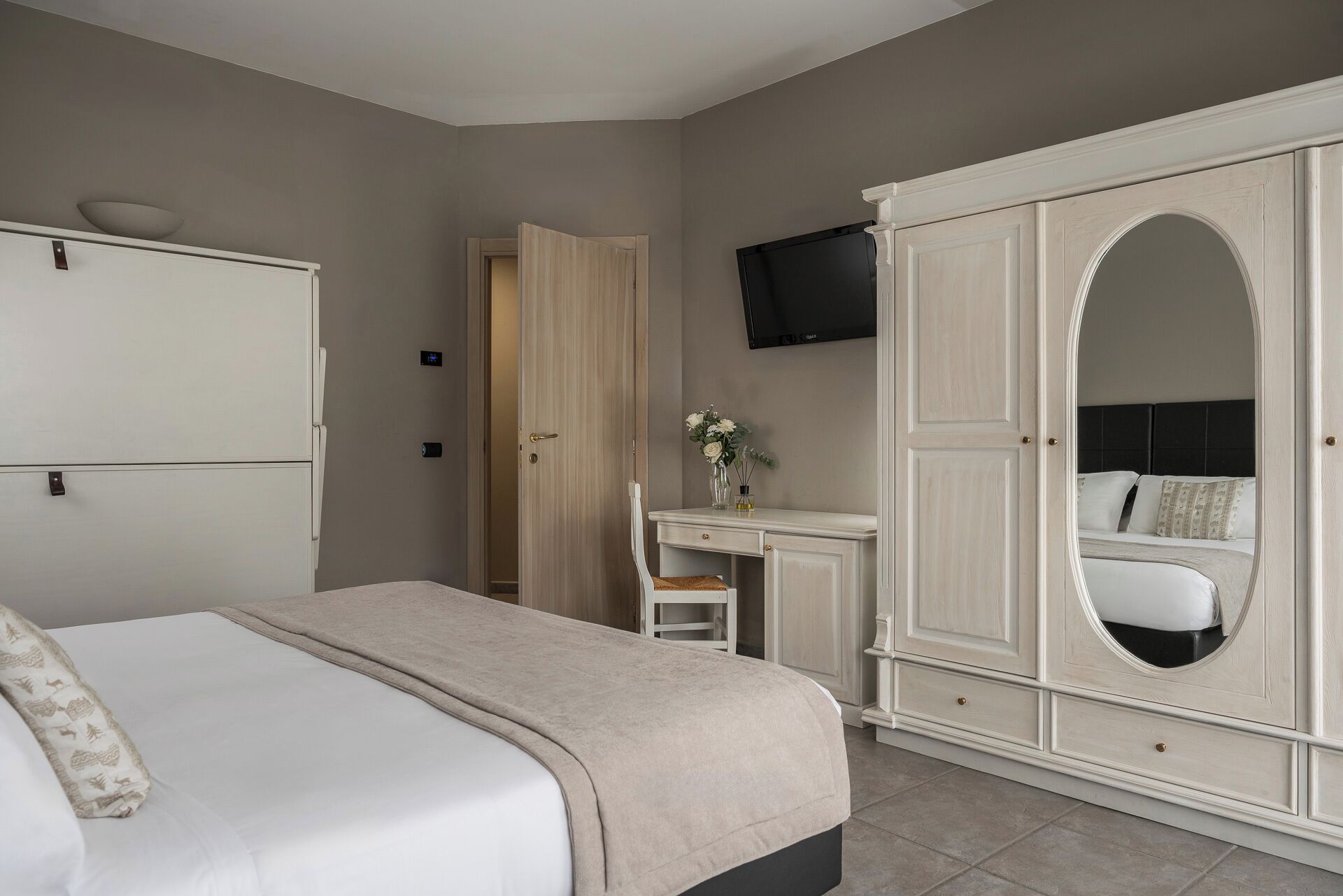 Quarto com cama, escrivaninha, guarda-roupa e televisão.