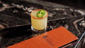 Um copo de cocktail com a borda mergulhada em sal, guarnecido com uma fatia de pimenta jalapeño, e um caderno de couro marrom com texto em relevo.