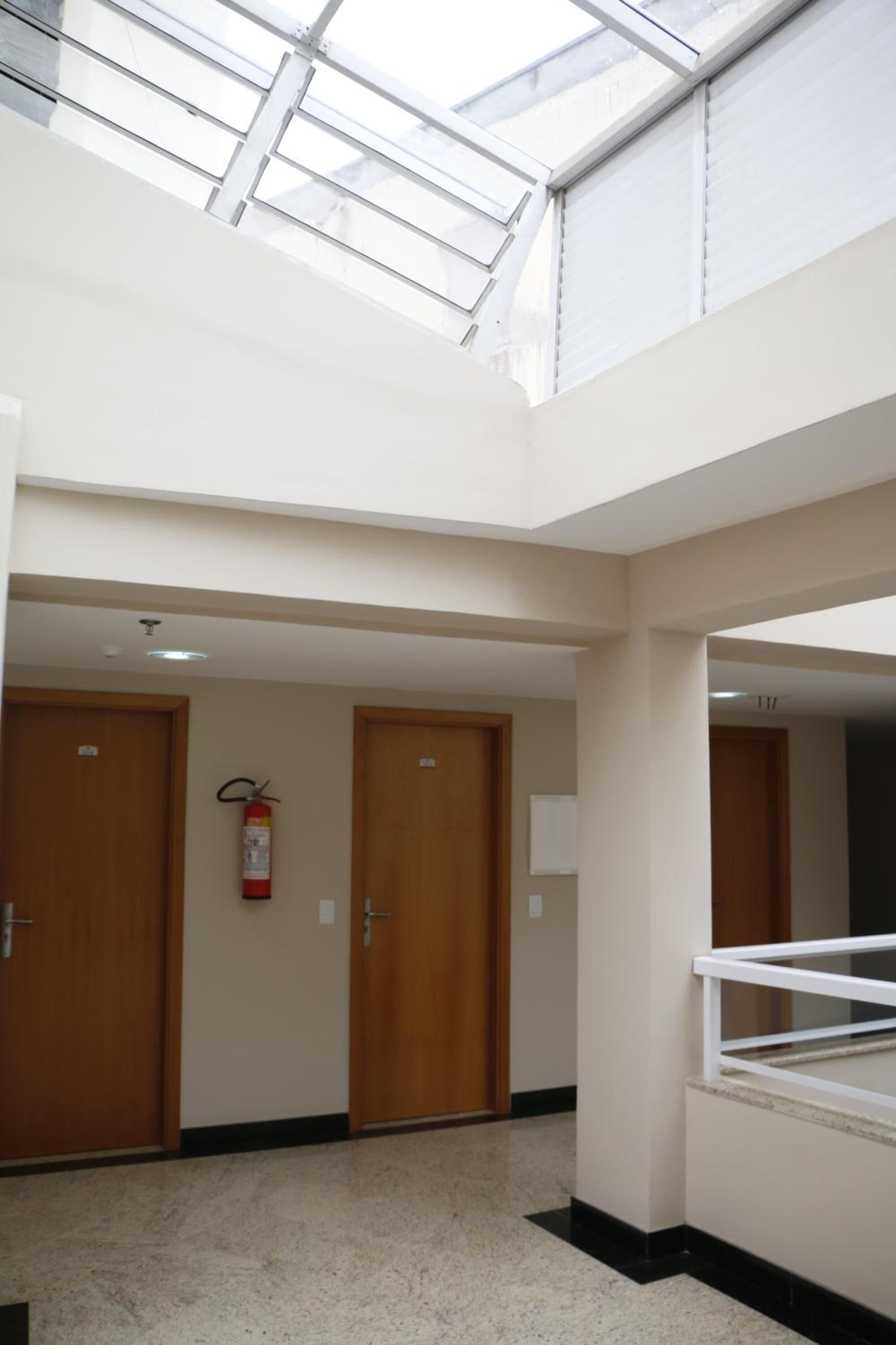 Interior com vários níveis, claraboia, portas de madeira, extintor de incêndio e corrimão branco.