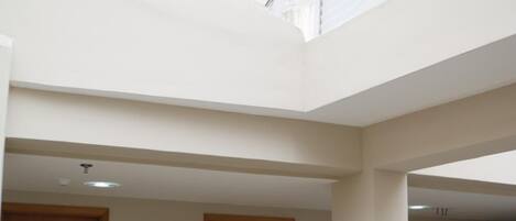 Interior com vários níveis, claraboia, portas de madeira, extintor de incêndio e corrimão branco.