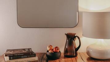 Uma mesa de madeira com um espelho, livros, um jarro e uma tigela de frutas.