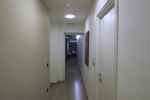 Um corredor estreito com piso de madeira, paredes brancas e uma porta à direita.