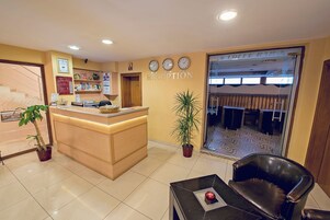 Uma área de recepção com balcão, planta em vaso, relógio e espaço de estar com uma cadeira.