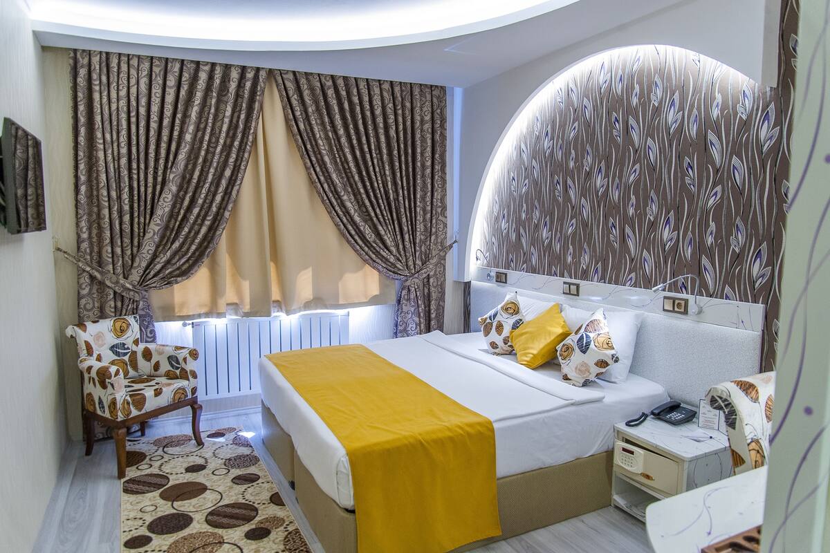 Quarto de hotel com uma cama, uma cadeira, uma mesinha de cabeceira e um espelho decorativo grande.