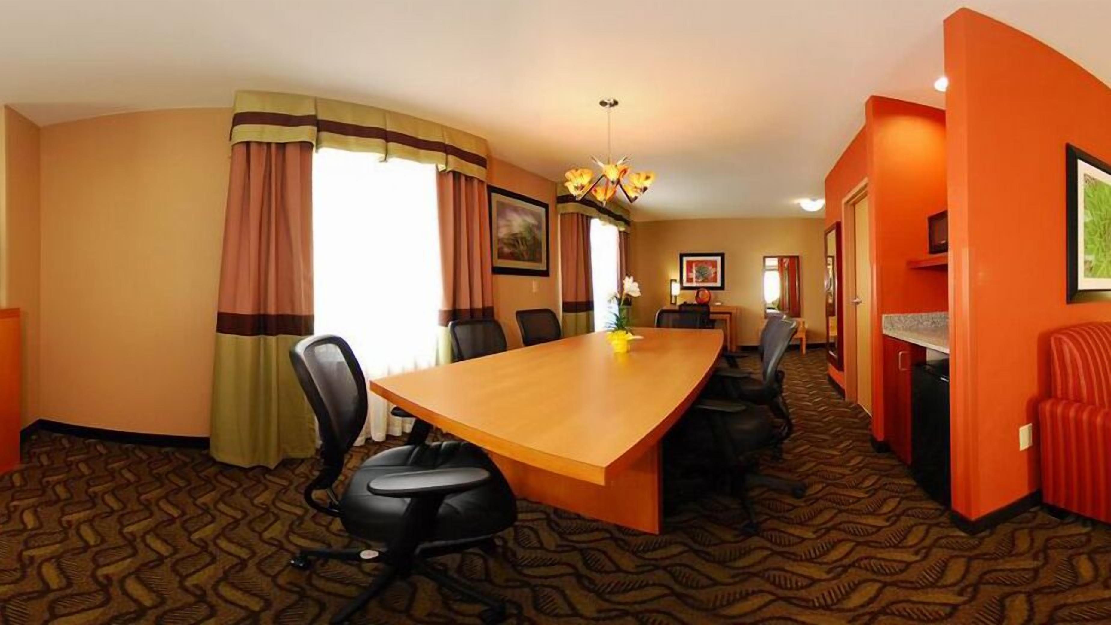 Uma sala de conferências de hotel com uma mesa comprida, várias cadeiras, um candelabro e um tapete estampado.