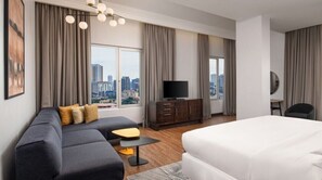 Quarto de hotel moderno com uma cama grande, um sofá, uma TV e vista para a cidade.
