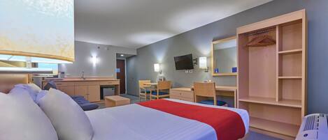 Quarto de hotel com cama, escrivaninha, cadeira, guarda-roupa e televisão.