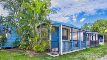 Uma casa azul de dois andares com varanda, rodeada por vegetação tropical.