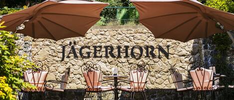 Pareda de pedra com o nome "Jägerhorn" e área externa com mesas e guarda-sóis.