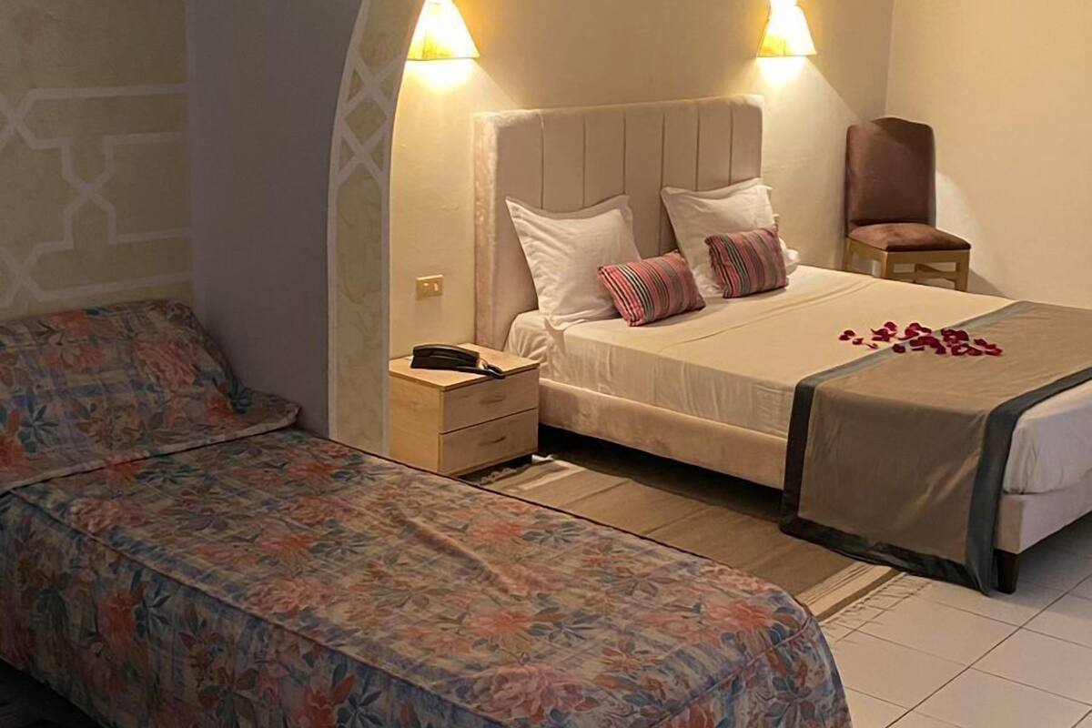 Quarto com duas camas, mesa de cabeceira, uma cadeira e um arco decorativo.