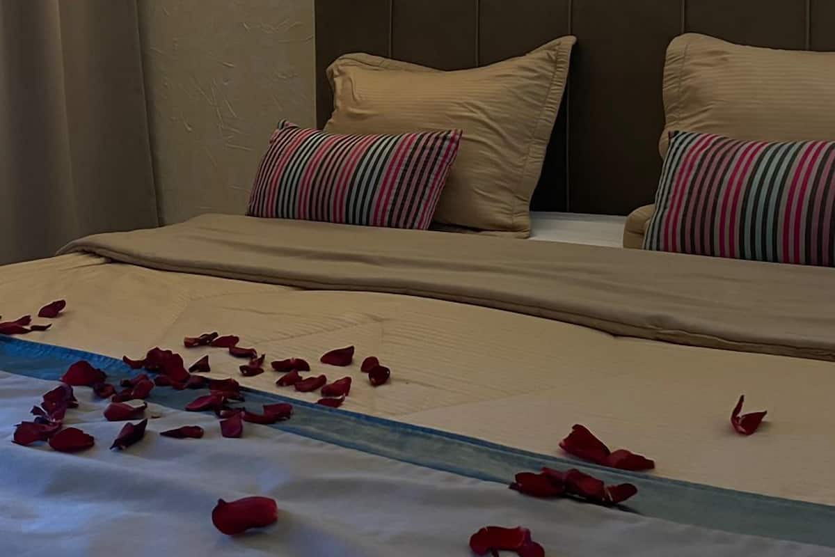 Quarto de hotel com cama, almofadas e luminária fixada na parede.