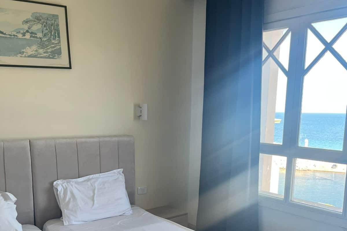 Quarto de hotel com cama, janela com vista para o mar e um quadro na parede.