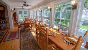 Uma sala de jantar com uma mesa de madeira comprida, várias cadeiras e um ventilador de teto.