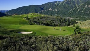 Um campo de golfe com vista panorâmica para montanhas e uma pequena cidade ao fundo.