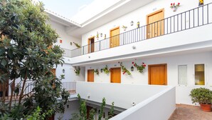 Pátio com vários níveis, paredes brancas, portas de madeira e plantas em vasos.
