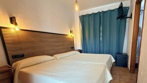 Uma cama de casal com cabeceira de madeira, mesa de cabeceira, luminária fixada na parede e cortina azul.