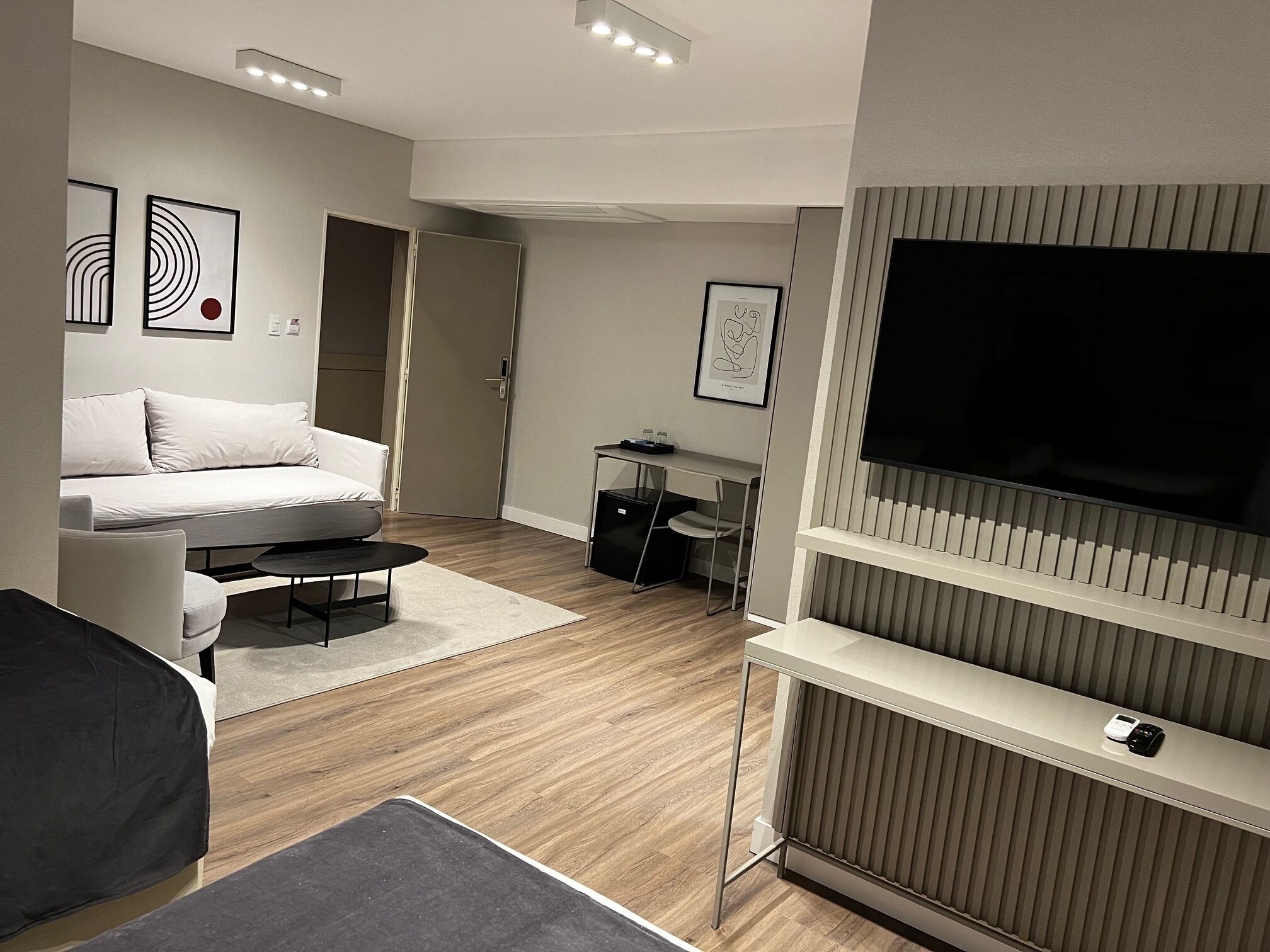 Quarto de hotel moderno com cama, escrivaninha, cadeira, televisão e obras de arte nas paredes.
