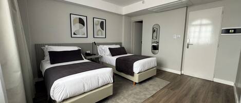 Quarto de hotel moderno com duas camas, um espelho e uma porta.
