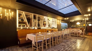 Restaurante com teto alto, piso estampado e área de bar com prateleiras e assentos.