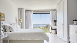 Quarto de hotel moderno com uma cama grande, uma escrivaninha e vista para o mar.