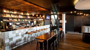 Uma área de bar com um balcão comprido, banquetas e diversas garrafas nas prateleiras.