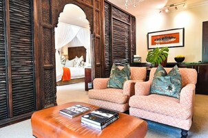 Quarto com uma cama, duas poltronas, uma mesa de centro e um quadro na parede.