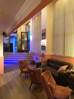 Uma sala de estar moderna com um sofá, duas poltronas e uma mesa de centro. Escadas levam a um andar superior, e uma planta é visível nos degraus.