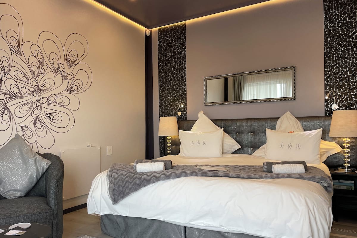 Quarto moderno com uma cama grande, arte decorativa na parede, um espelho e duas luminárias de cabeceira.