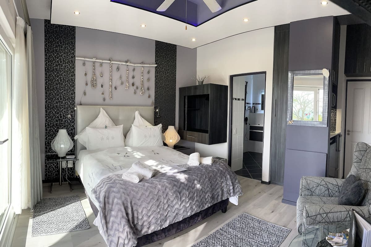Quarto moderno com uma cama grande, televisão e área de estar com uma poltrona.