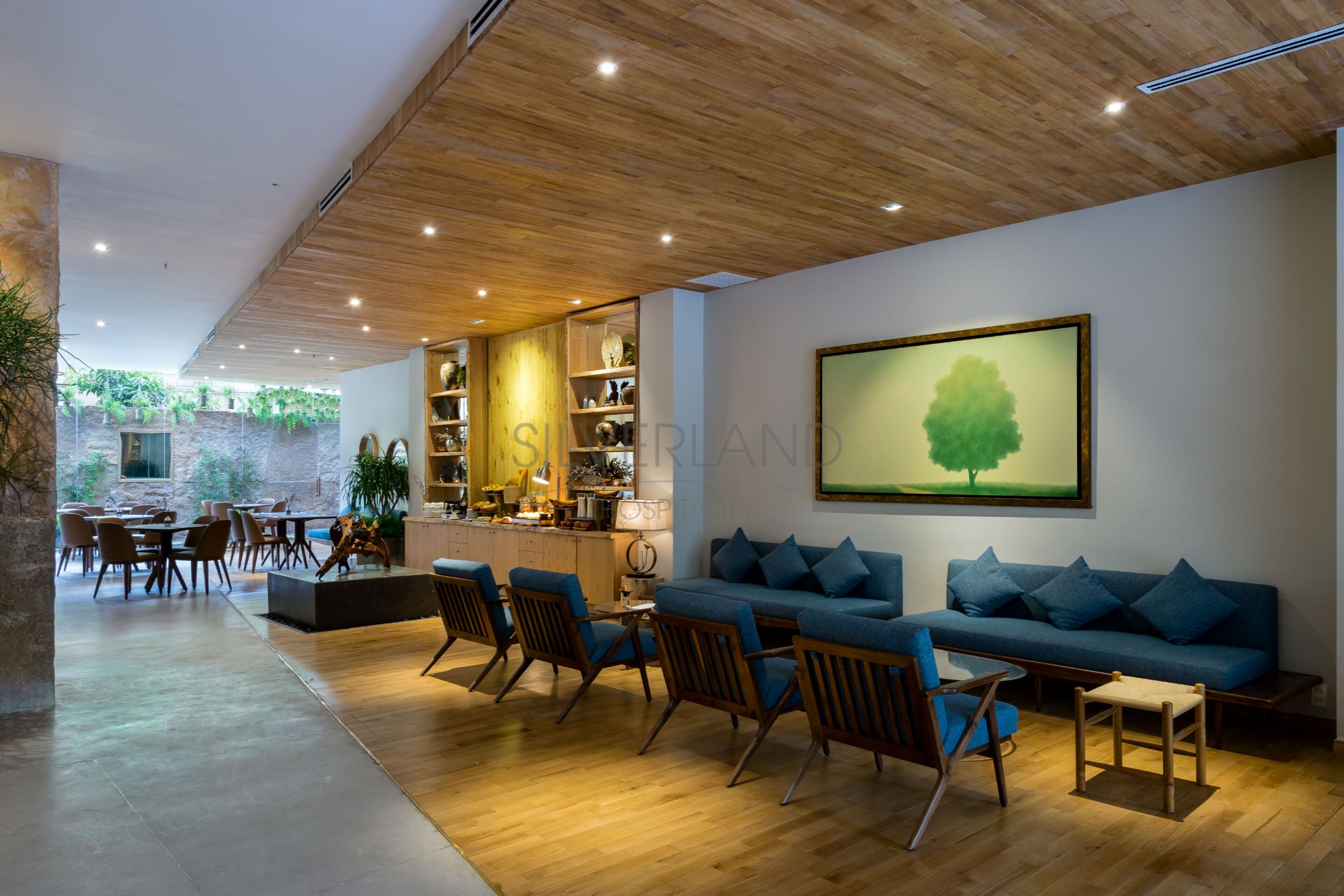 Um interior moderno com teto de madeira, um conjunto de sofá azul e uma área de refeições com cadeiras e mesas.