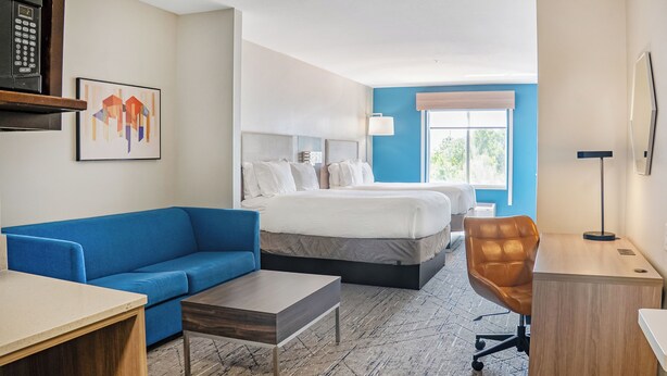 Quarto de hotel com um sofá azul, uma cama com roupa de cama branca, uma escrivaninha de madeira e uma cadeira.