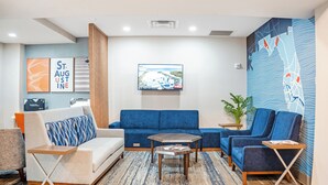Um hall de hotel moderno com um sofá azul, um sofá branco, uma mesa de centro de madeira e uma poltrona azul.