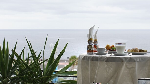 Uma mesa com vista para o mar, uma planta e uma disposição para café da manhã, incluindo uma xícara, prato e saleiro e pimenteiro.