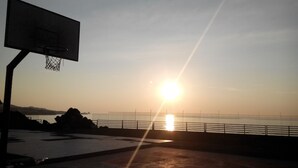 Uma quadra de basquete com rede, cerca e um corpo d'água ao fundo.