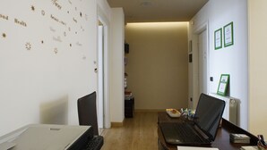 Um escritório em casa com uma mesa, dois laptops e uma cadeira. Uma estante está ao fundo.