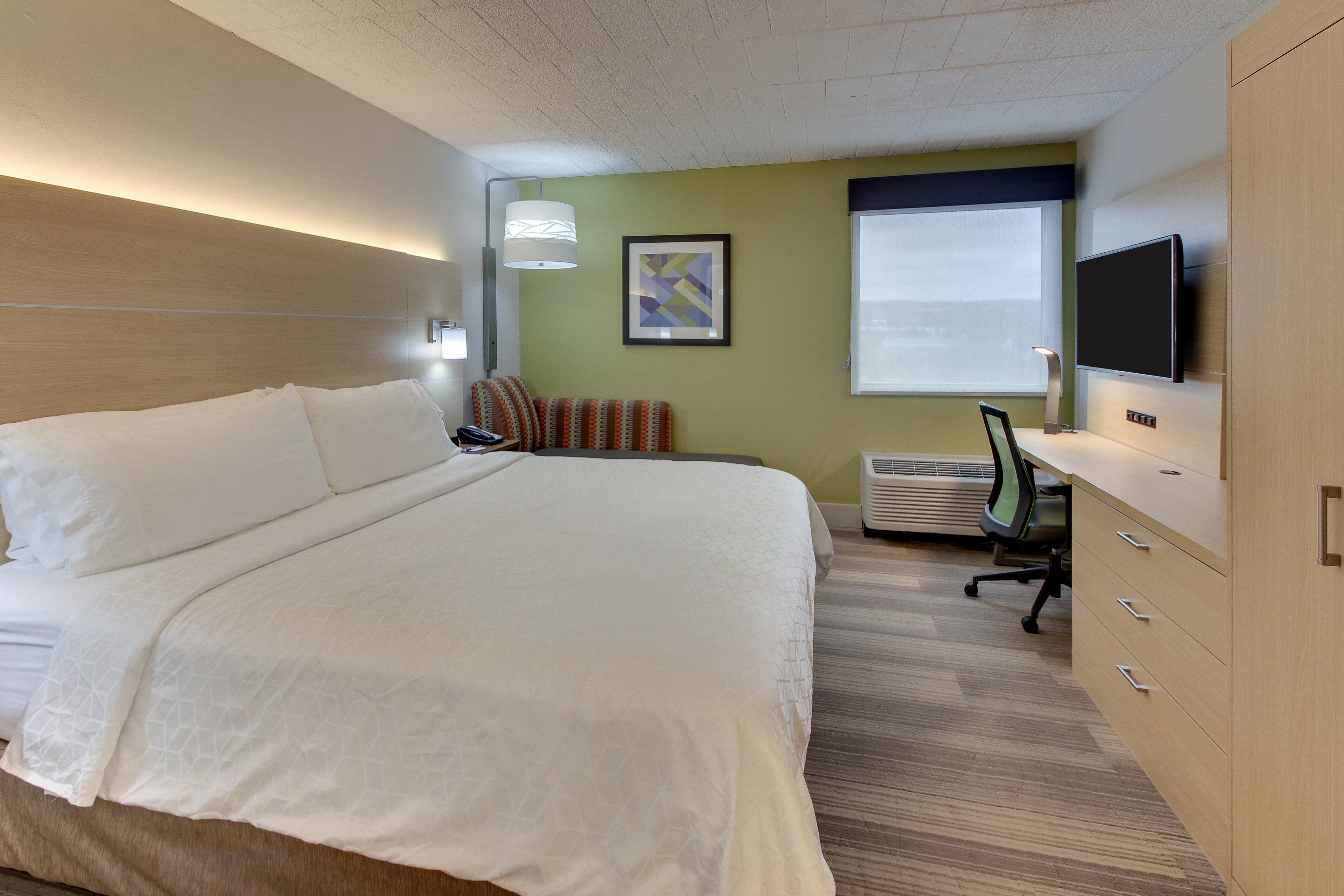 Quarto de hotel com uma cama grande, uma escrivaninha com computador, televisão e janela com vista.