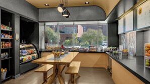 Interior moderno de café com mesa e bancos de madeira, balcão refrigerado e vista para a rua.