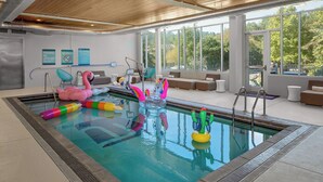 Piscina com brinquedos infláveis coloridos, uma cadeira de salva-vidas e vista para o exterior através de grandes janelas.