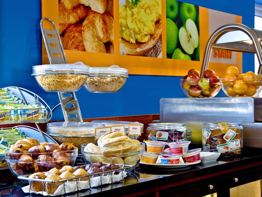 Buffet com diversos itens de comida, incluindo doces, frutas e cereais.