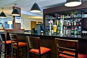 Uma área de bar com cadeiras de madeira, balcão e diversas garrafas de bebidas alcoólicas.