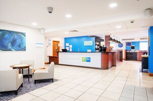Área de recepção de hotel com parede azul, balcão de atendimento e disposição de assentos.