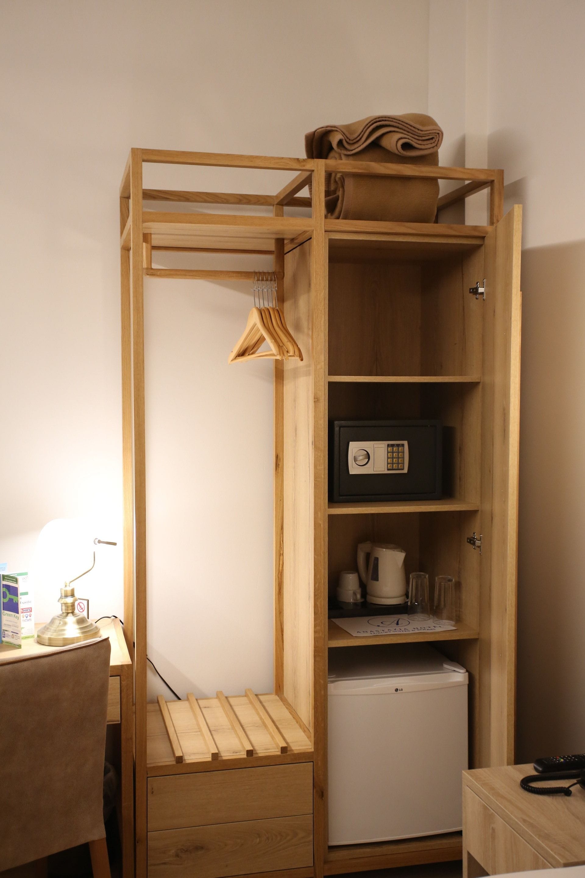 Quarto compacto de madeira com roupeiro embutido, pequena geladeira e área de trabalho com luminária e telefone.