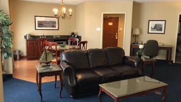 Sala de estar com sofá de couro, mesa de centro de vidro, área de jantar com mesa e cadeiras de madeira, e cozinha ao fundo.