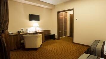 Quarto de hotel com escrivaninha, cadeira, cama e televisão fixada na parede.
