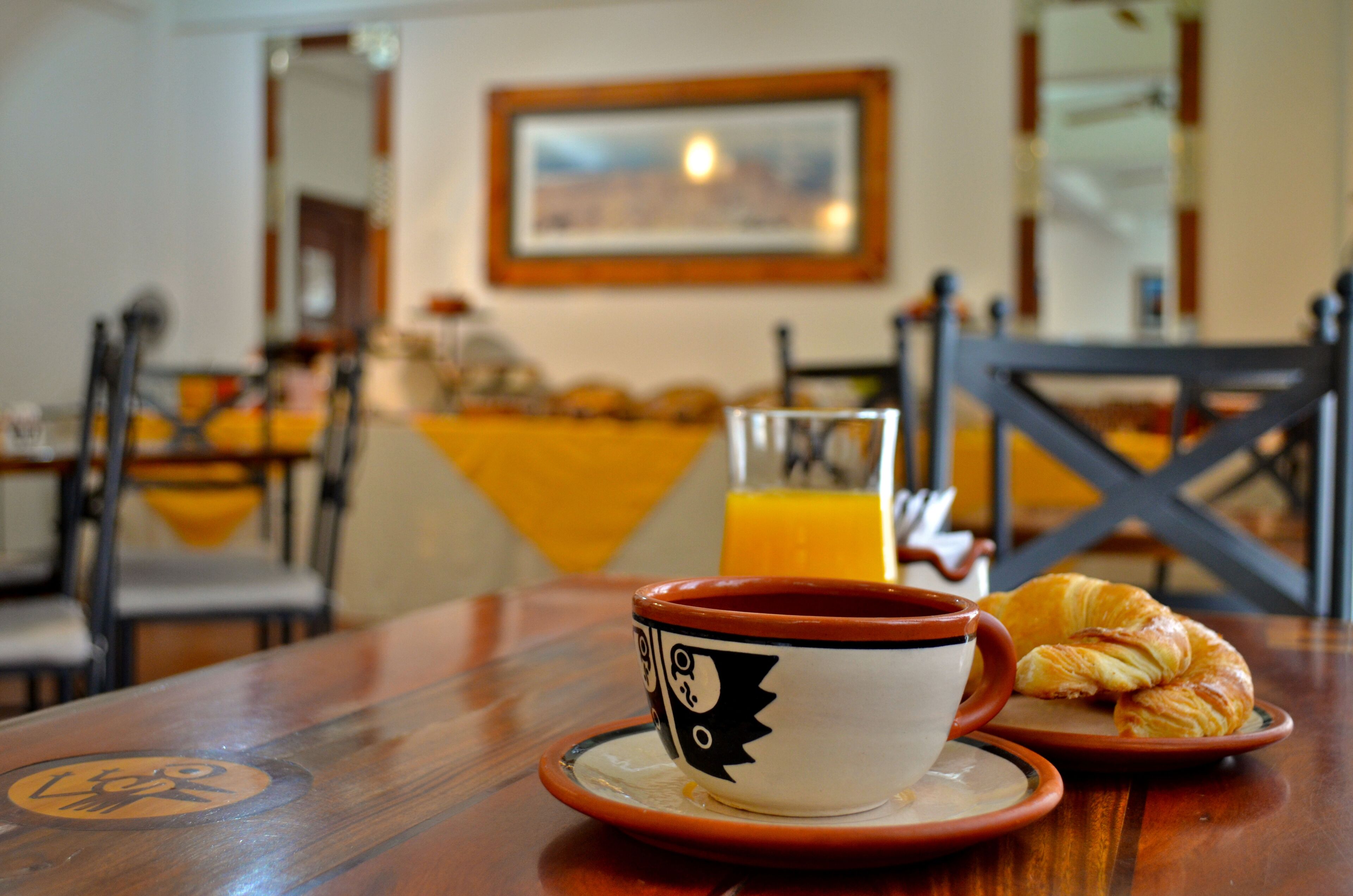 Disposição para o café da manhã com uma xícara, croissant e suco de laranja sobre uma mesa de madeira.