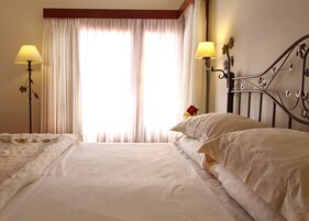 Quarto de hotel com duas camas, uma janela grande com cortinas translúcidas e luminárias fixadas na parede.